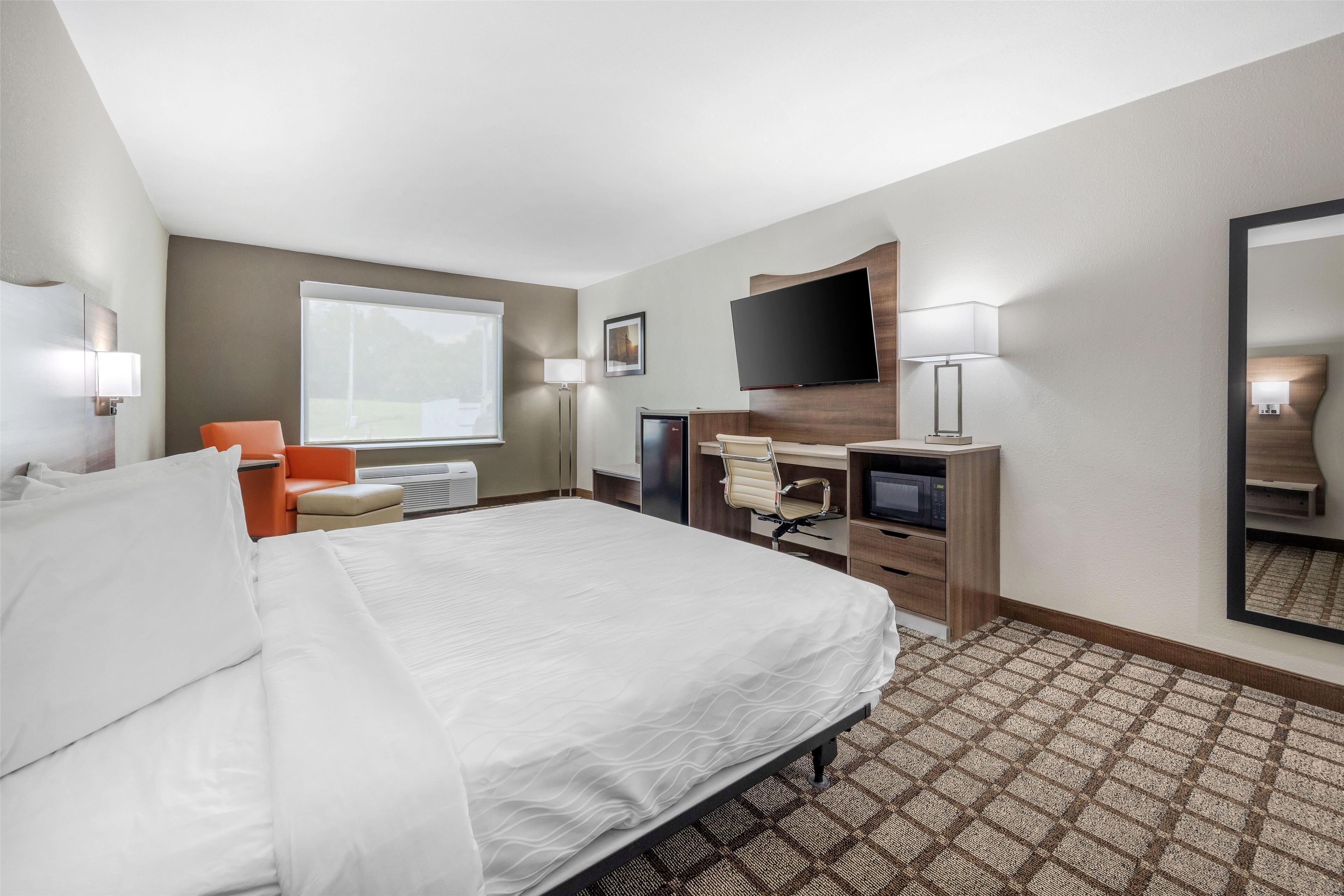 Quarto de hotel com uma cama grande, uma escrivaninha com computador, uma cadeira, televisão de tela plana e uma janela.