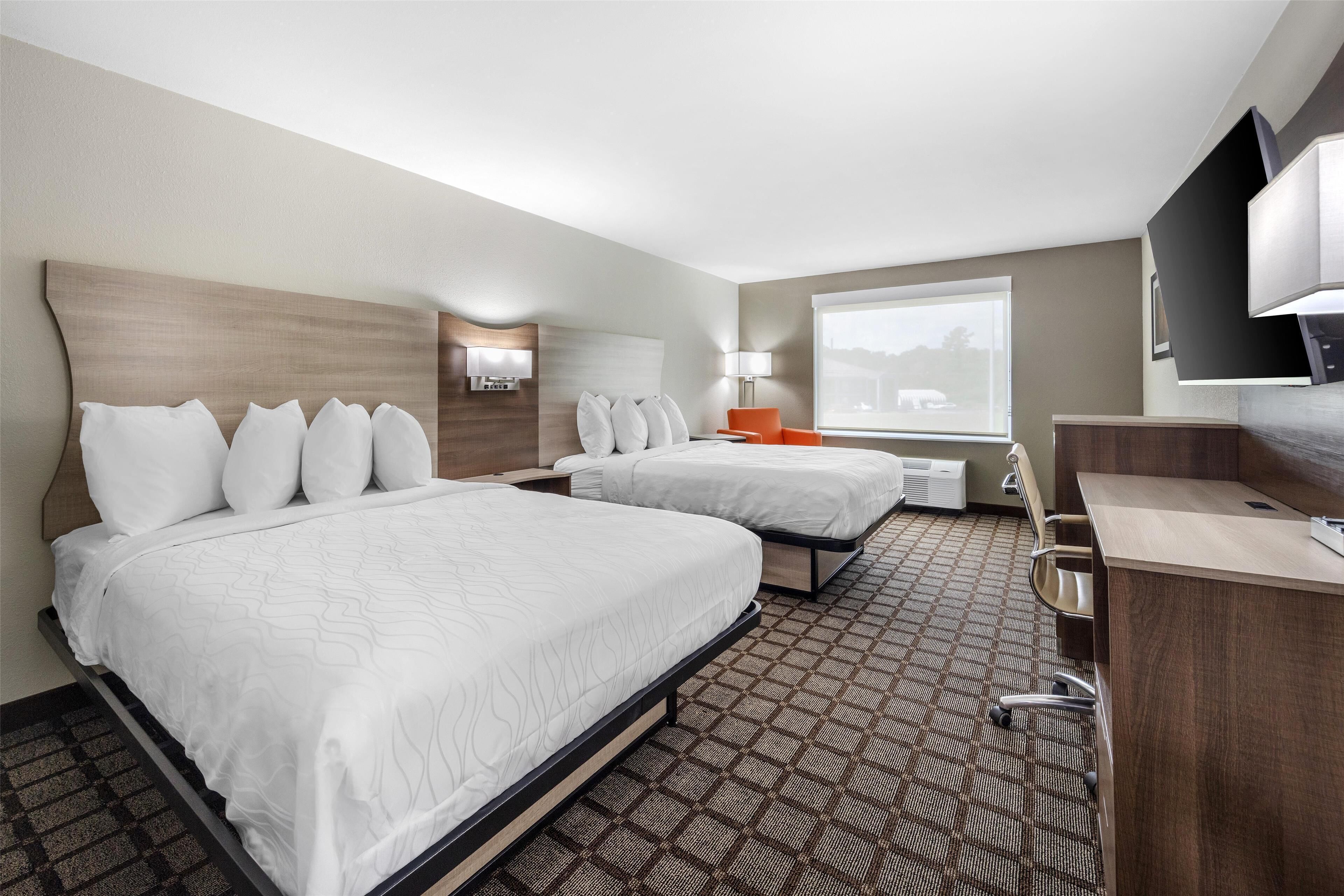 Quarto de hotel com duas camas, uma escrivaninha, uma cadeira, uma televisão e uma janela.