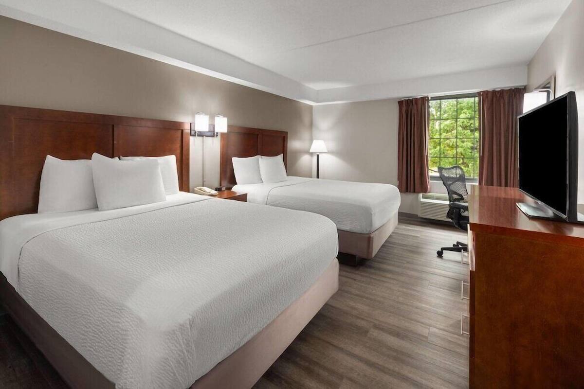 Quarto de hotel com duas camas, uma escrivaninha, televisão e janela com cortinas.