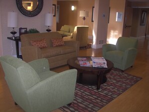 Sala de estar com sofá, duas poltronas, mesa de centro com revistas e tapete estampado.