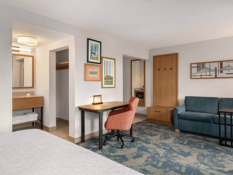 Quarto de hotel com escrivaninha, cadeira, sofá e guarda-roupa.