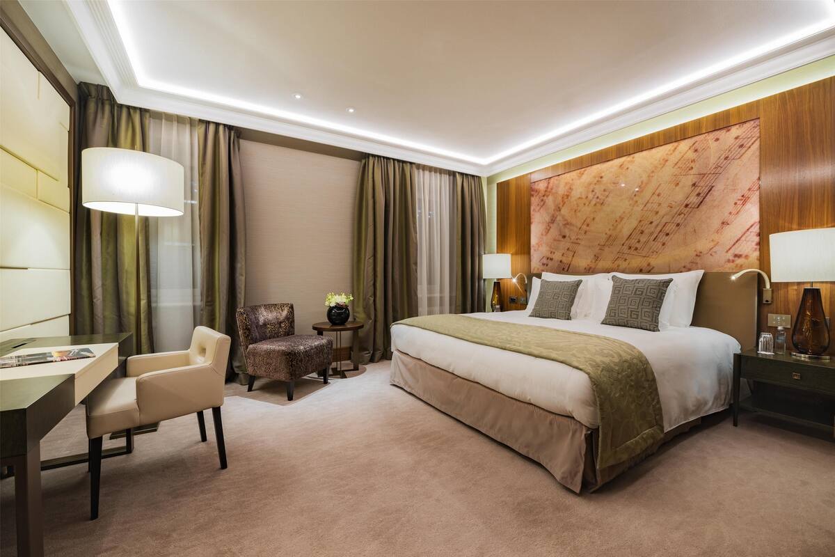 Quarto de hotel com uma cama grande, uma escrivaninha, uma cadeira e uma pequena mesa com abajur.