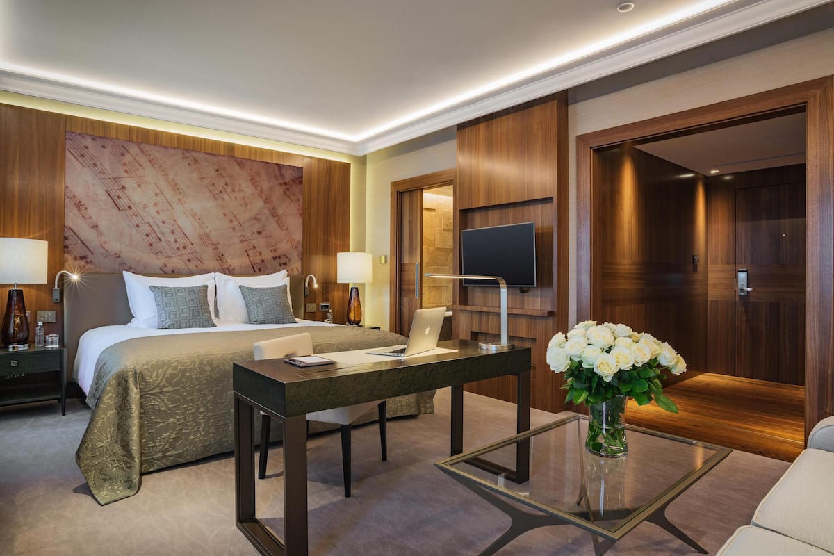 Quarto de hotel moderno com uma cama grande, uma escrivaninha com um laptop, uma TV e um vaso de flores.