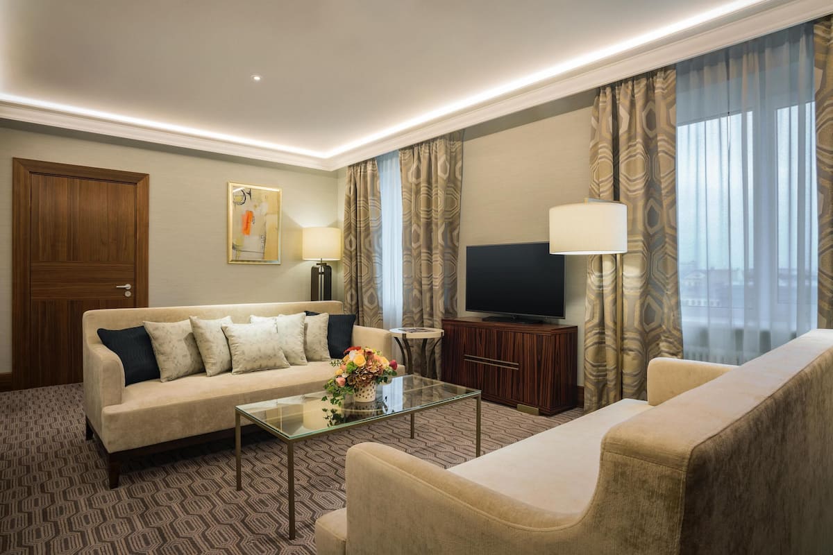 Quarto de hotel com sofá, mesa de centro de vidro, televisão e armário.