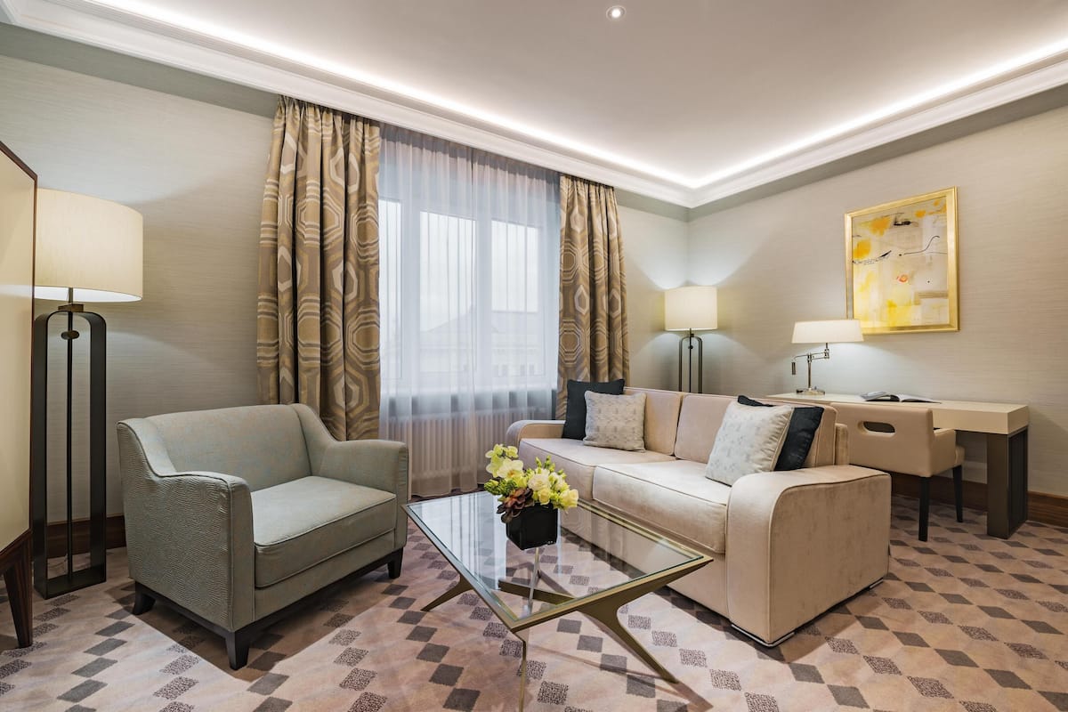 Uma sala de estar moderna com sofá, poltrona, mesa de centro de vidro e escrivaninha com abajur.