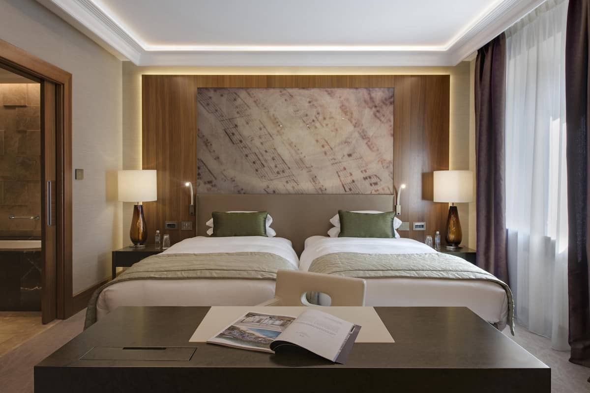 Quarto de hotel com duas camas, uma grande obra de arte abstrata na parede e uma escrivaninha com uma revista.