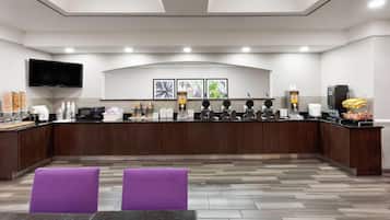 Um hall de hotel moderno com uma mesa de recepção, uma TV de tela plana e uma área de estar com cadeiras roxas.