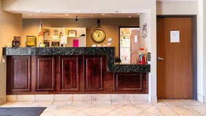 Uma área de recepção de hotel com balcão de mármore, armários de madeira, um relógio e uma porta com a inscrição 'Apenas Funcionários do Hotel'.
