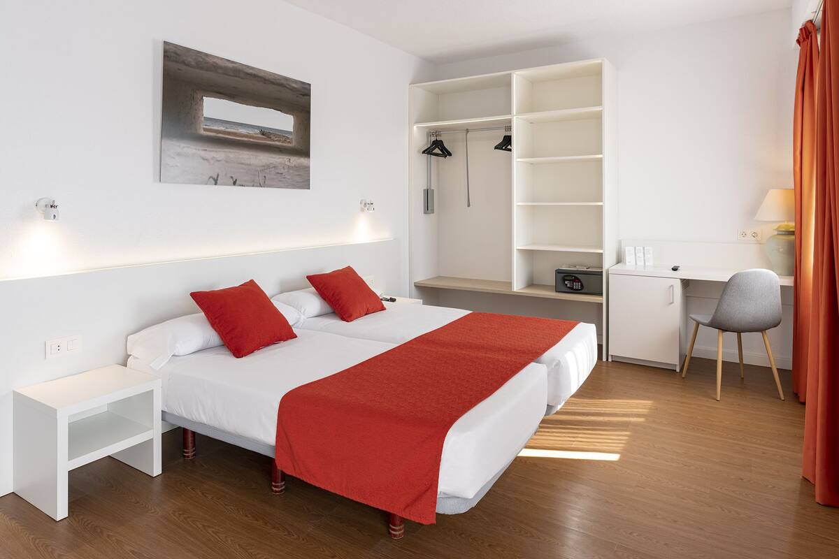 Quarto de hotel com cama, escrivaninha, cadeira e guarda-roupa.