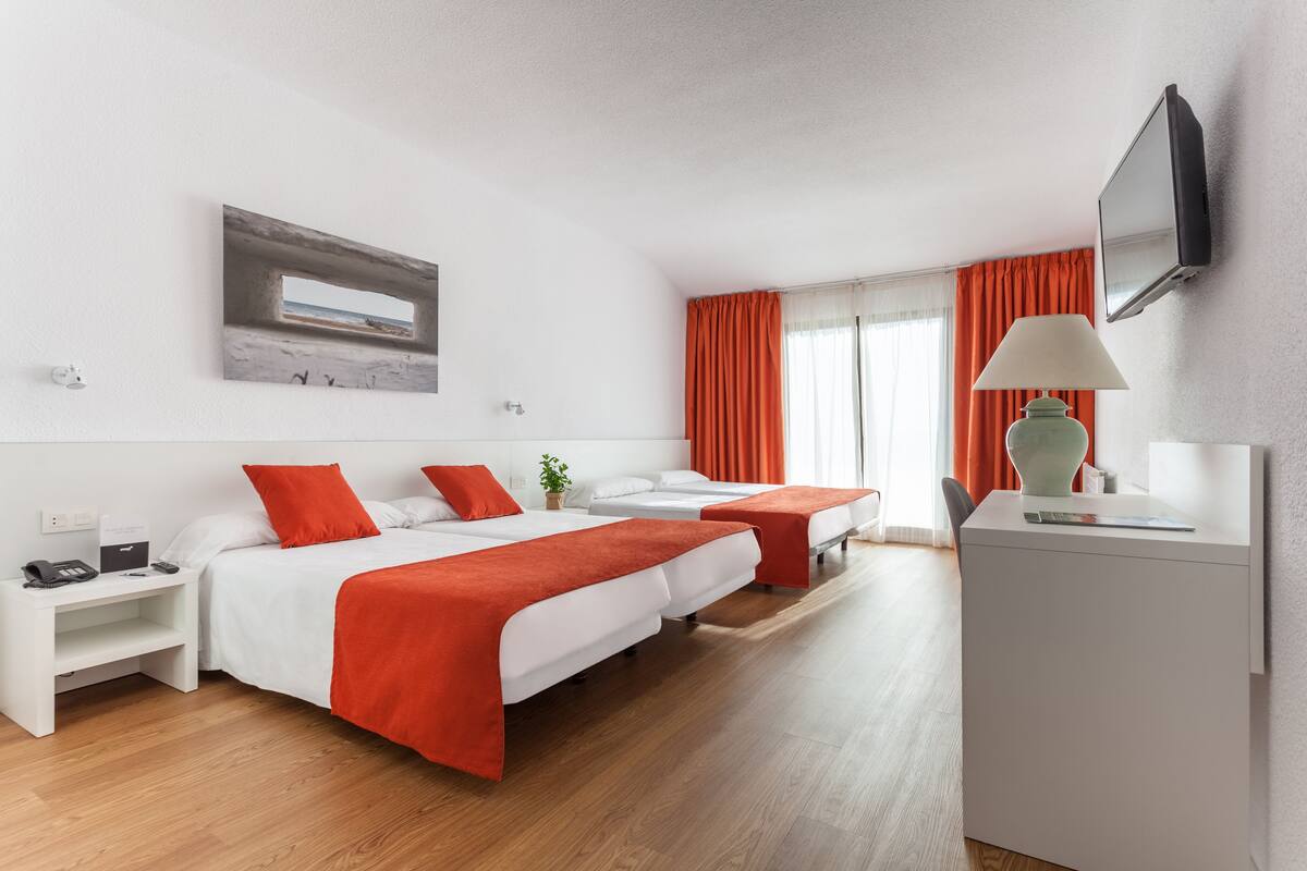 Quarto de hotel com duas camas, uma escrivaninha, uma televisão e uma janela com cortinas.