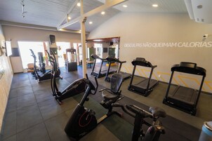 Academia com diversos equipamentos de cardio, incluindo esteiras e bicicletas ergométricas, e uma parede com frases motivacionais.