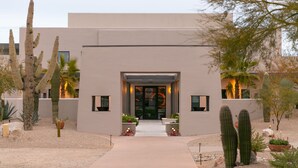 Um edifício moderno com entrada central, rodeado por cactos e plantas típicas do deserto.