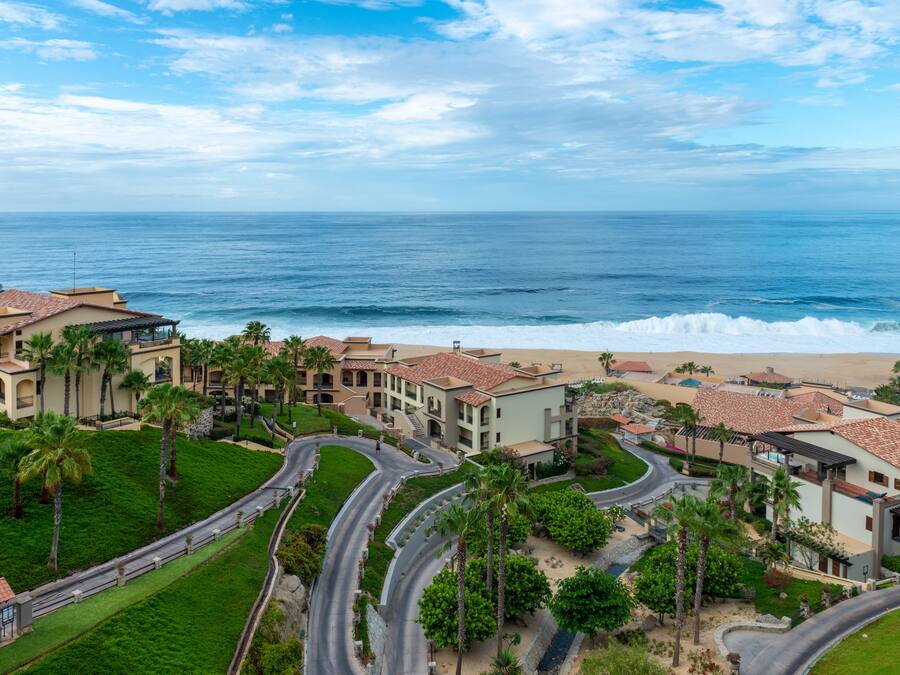 Um resort costeiro com vários edifícios, estradas sinuosas e vista para a praia.