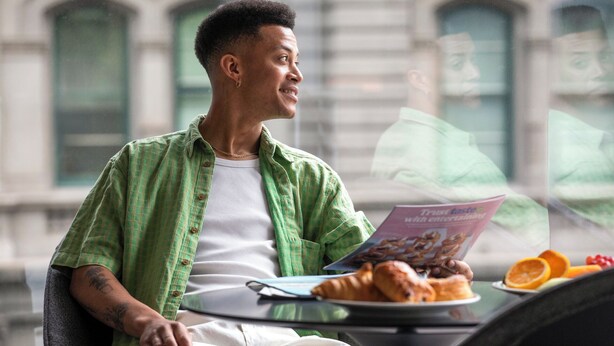 Uma pessoa sentada à mesa com um laptop, uma revista e um croissant.