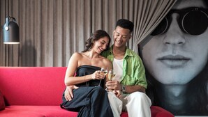 Um casal sentado em um sofá vermelho, com um grande retrato ao fundo.