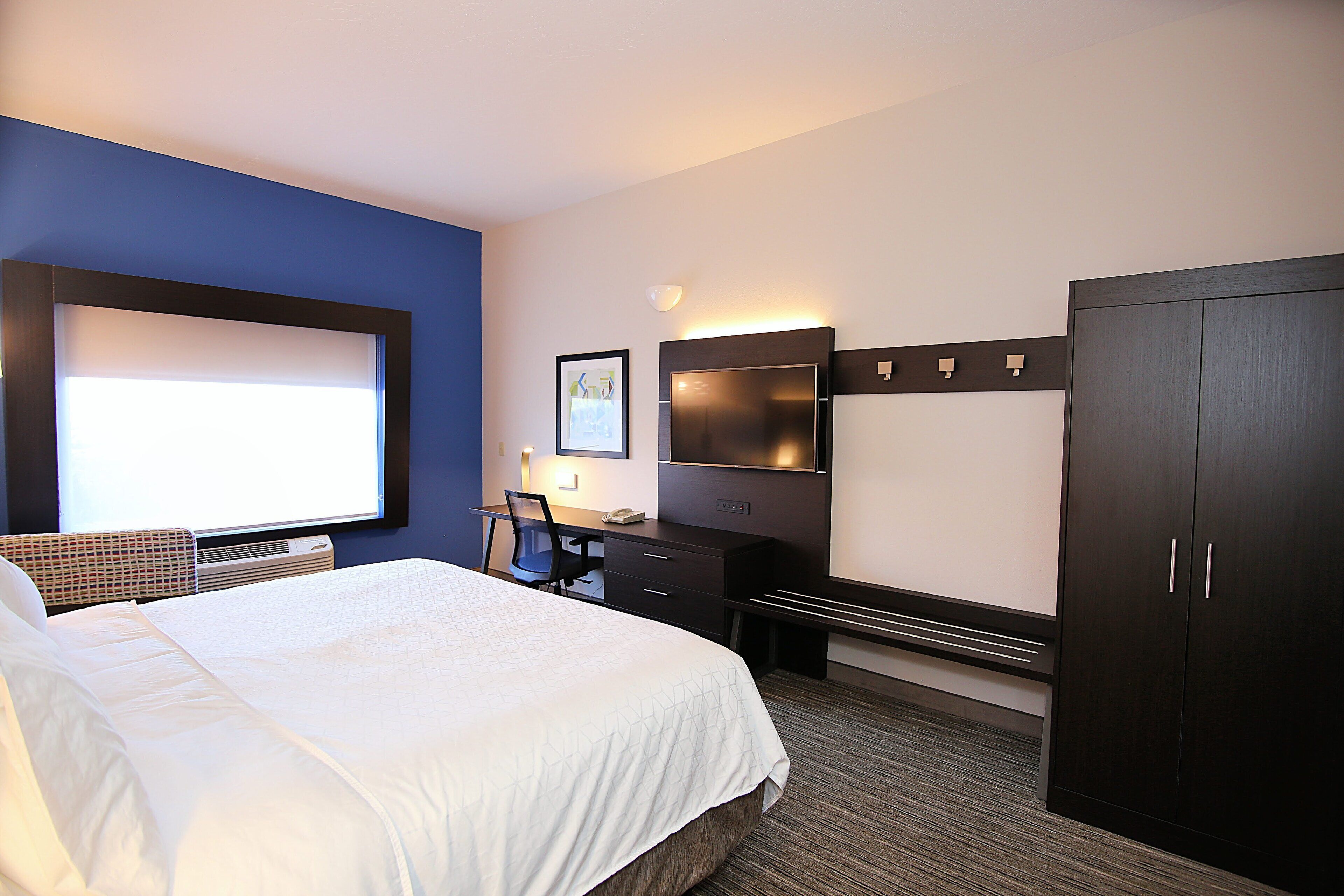 Quarto de hotel com uma cama grande, uma escrivaninha com cadeira, um guarda-roupa e uma televisão.