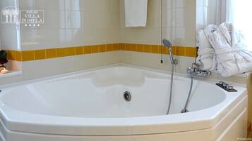 Uma banheira branca com chuveiro, um porta-toalhas com toalhas e uma parede revestida de azulejos amarelos.