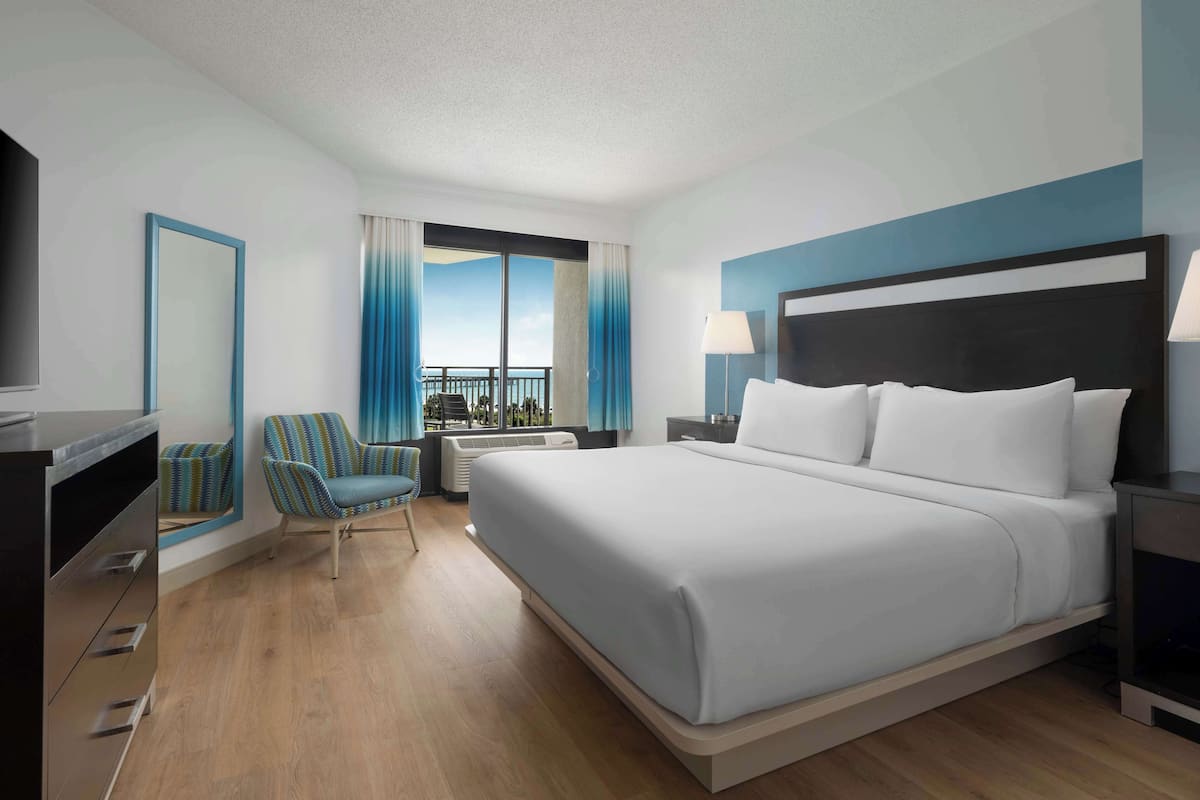 Quarto de hotel com uma cama grande, uma mesa, uma cadeira, uma TV e uma varanda com vista.