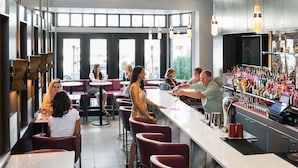 Uma área de bar moderna com assentos e balcão, exibindo diversas garrafas e uma tela digital.