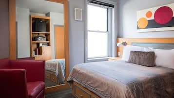 Quarto de hotel com uma cama, uma cadeira vermelha, um guarda-roupa, um espelho, uma janela e um quadro na parede.