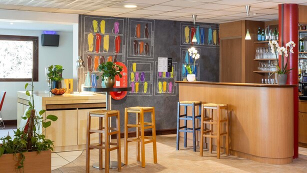 Uma área de bar com banquetas, balcão e parede com vasos coloridos.