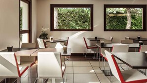 Uma área de jantar moderna com várias mesas e cadeiras, grandes janelas com vista para o verde e um design limpo e contemporâneo.