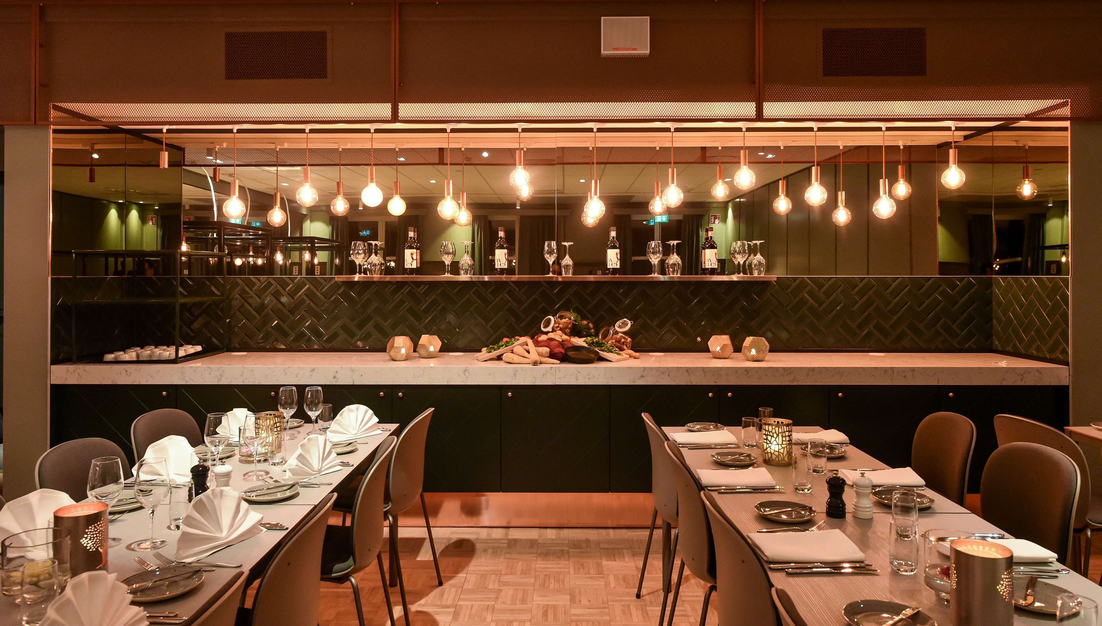 Restaurante com balcão extenso, lâmpadas penduradas e painel de fundo espelhado.