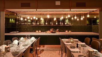 Restaurante com balcão extenso, lâmpadas penduradas e painel de fundo espelhado.