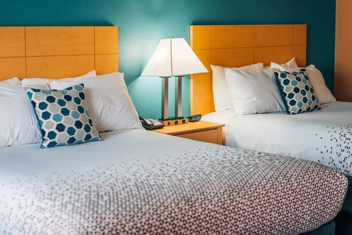 Quarto de hotel com duas camas, uma mesa de cabeceira com abajur e um telefone.