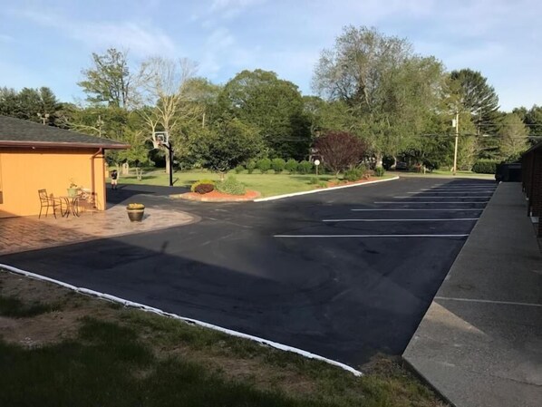 Um estacionamento com um edifício à esquerda, rodeado por árvores e vegetação.