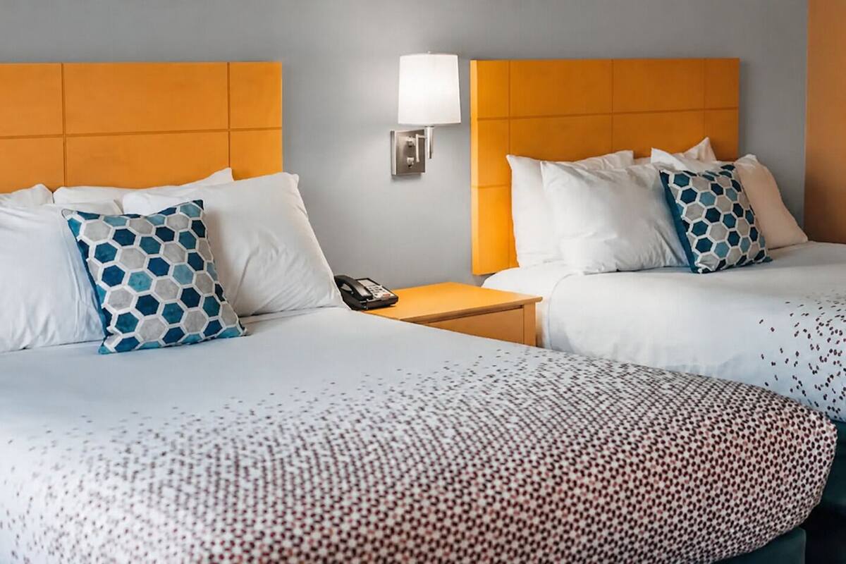 Quarto de hotel com duas camas, uma mesinha de cabeceira com telefone e uma luminária na parede.