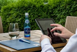 Uma pessoa usando um tablet em mesa externa, com um copo e garrafa de Perrier.