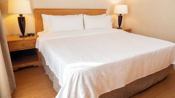 Uma cama bem arrumada com cabeceira de madeira, duas mesas de cabeceira com abajures e piso de madeira.