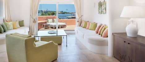 Uma sala de estar moderna com sofá, poltronas, mesa de centro e vista para o mar.