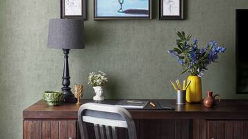 Uma mesa com uma cadeira, uma luminária, obras de arte emolduradas e um vaso com flores.