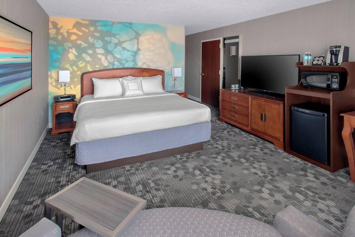 Quarto de hotel com cama grande, televisão de tela plana, micro-ondas, máquina de café e pequena geladeira.