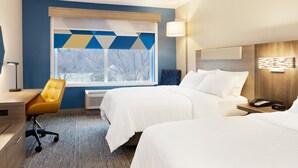 Quarto de hotel com duas camas, uma escrivaninha, uma cadeira e uma janela grande com vista para árvores.