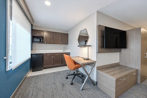 Quarto compacto com cozinha compacta, uma escrivaninha com cadeira, televisão na parede e porta de correr.