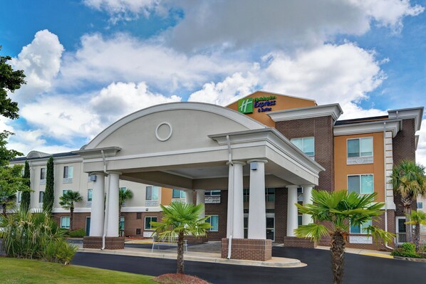 Um hotel Holiday Inn Express & Suites com design arquitetônico moderno, destacando uma entrada imponente com colunas e telhado plano.