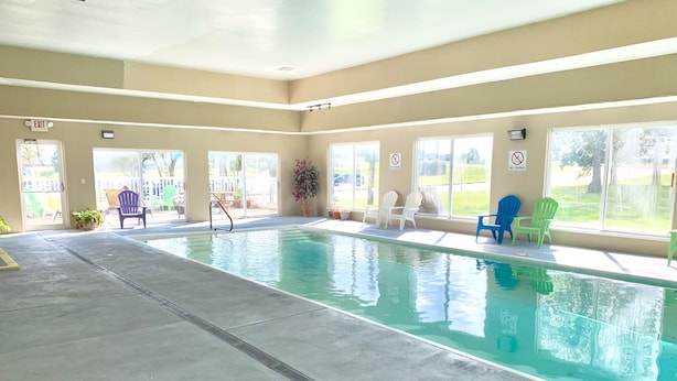 Uma piscina interior com paredes de vidro transparente, chão de concreto e várias cadeiras ao redor.