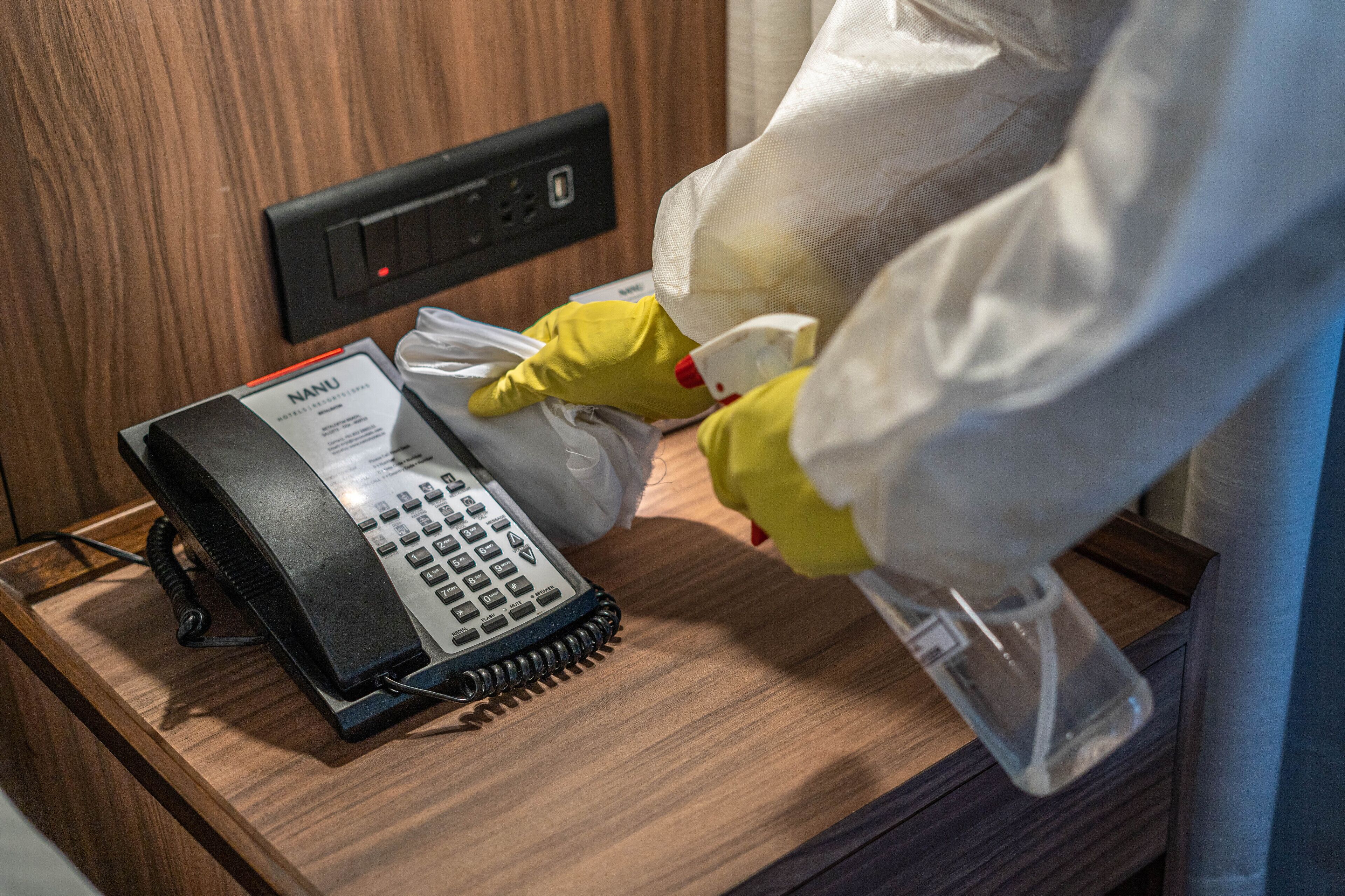 Quarto de hotel com uma secretária de madeira, um telefone e um saco plástico.