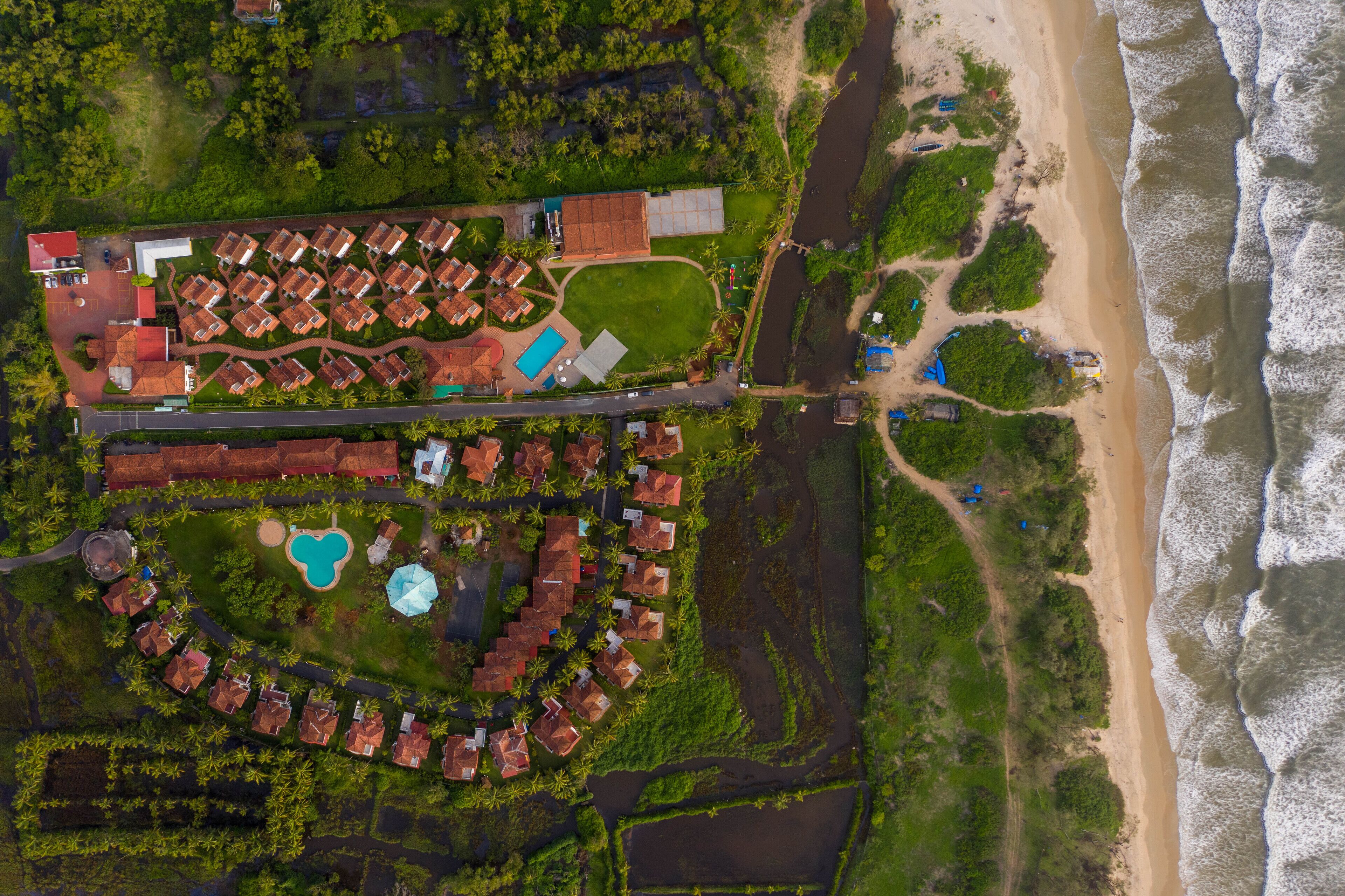 Vista aérea de um resort com vários edifícios tipo bangalô, uma piscina central e uma praia adjacente à propriedade.