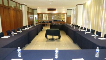 Sala de conferências com mesas compridas, cadeiras e garrafas de água.