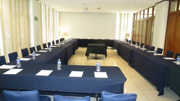 Uma sala de conferências com mesas compridas, cadeiras e garrafas de água.