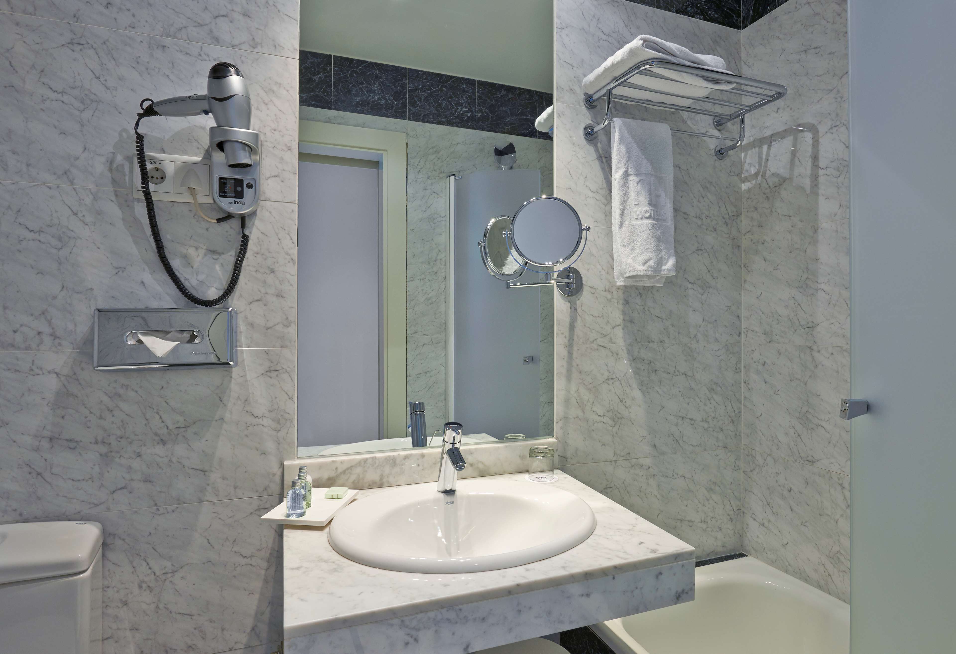Uma casa de banho com lavatório de mármore, secador de cabelo, espelho e porta-toalhas.