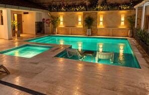Piscina com deck ladrilhado, cercada por vasos de plantas e iluminação embutida na parede.