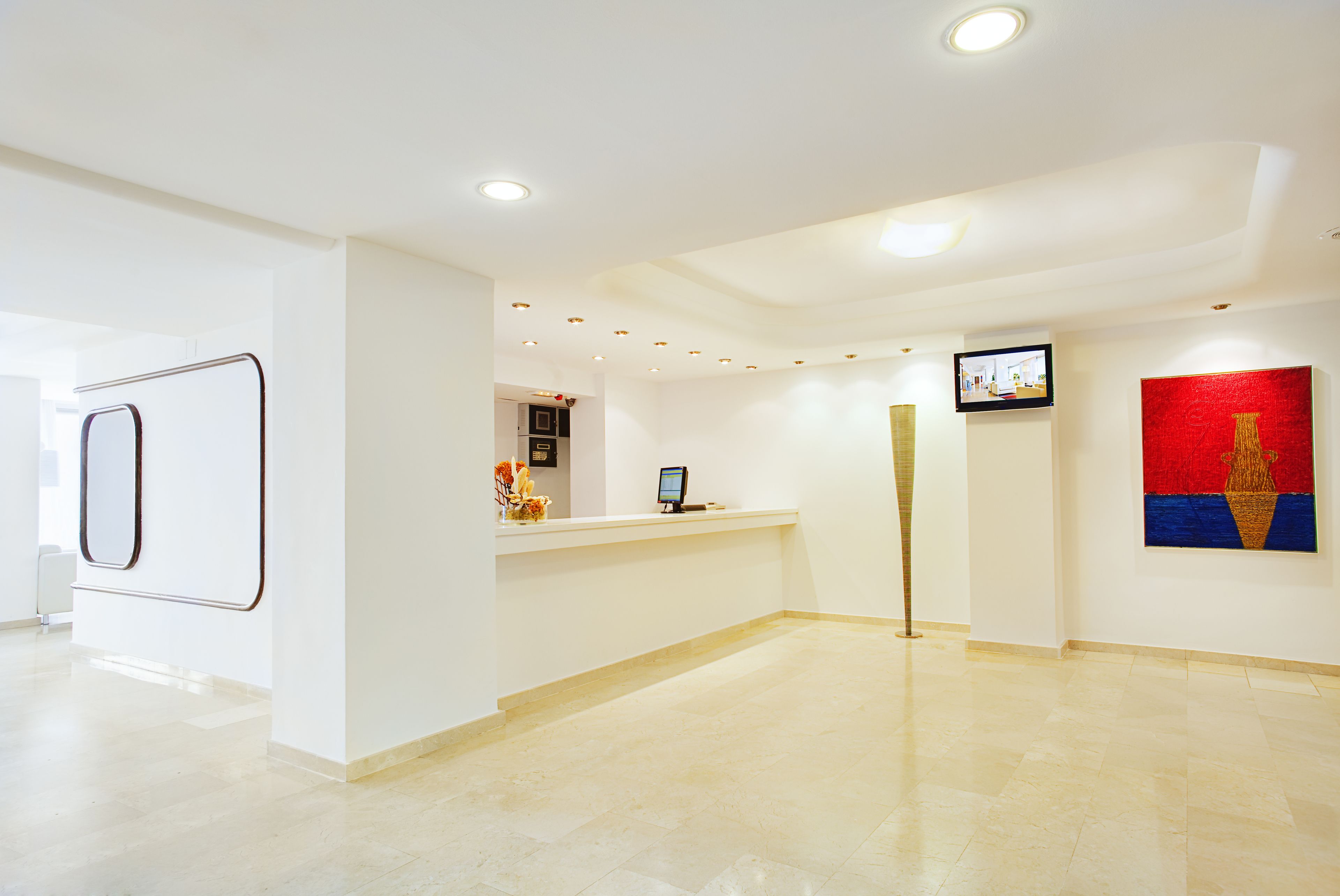 Uma área de recepção moderna, com um balcão branco, uma tela digital e uma obra de arte vermelha na parede.