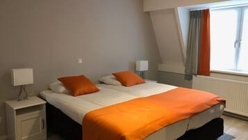 Quarto com cama, mesas de cabeceira e janela com cortinas.