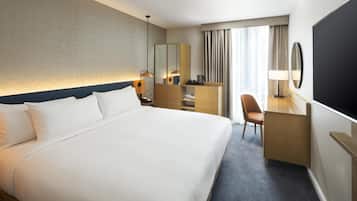 Quarto de hotel com uma cama grande, uma mesa, uma cadeira, uma televisão e uma janela com cortinas.