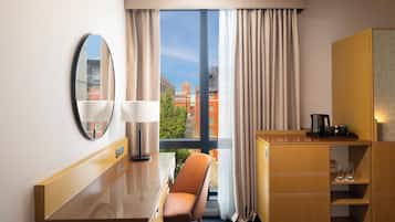 Quarto de hotel com secretária, cadeira e uma janela grande com cortinas.